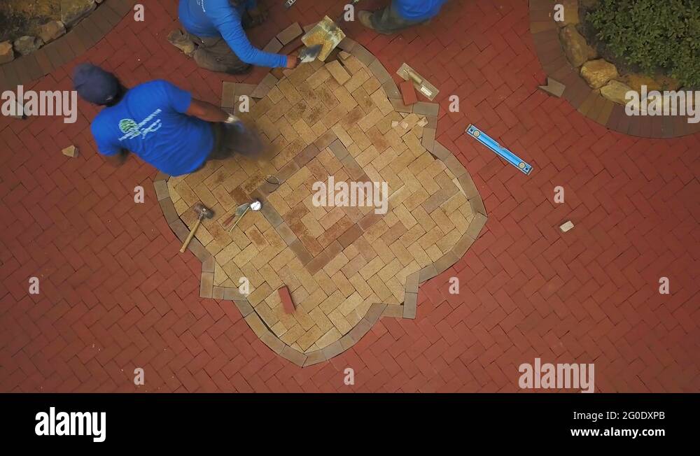 Two men work to try and fit the final bricks into a brick paver design ...