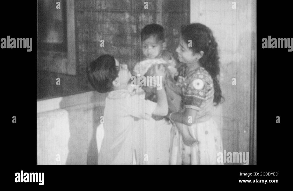 1950s: Boy and girl rock baby. Old man approaches and hands girl a jar ...