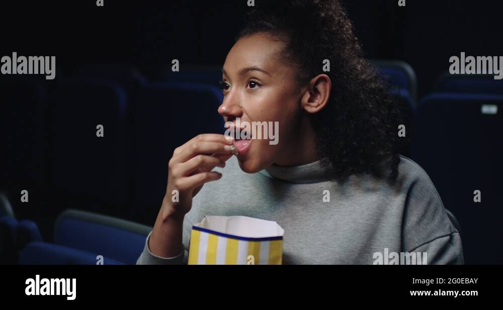 A woman sat in a movie theatre on her own eating popcorn, having fun ...
