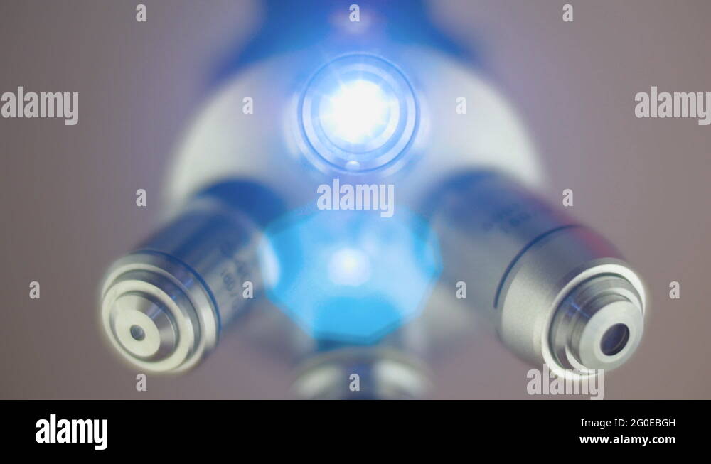A hand rotates a block of microscope lenses one of them glows brightly ...