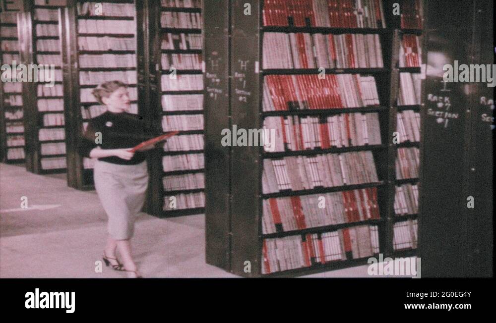 1950s: UNITED STATES: lady in library. Lady places record in vault ...