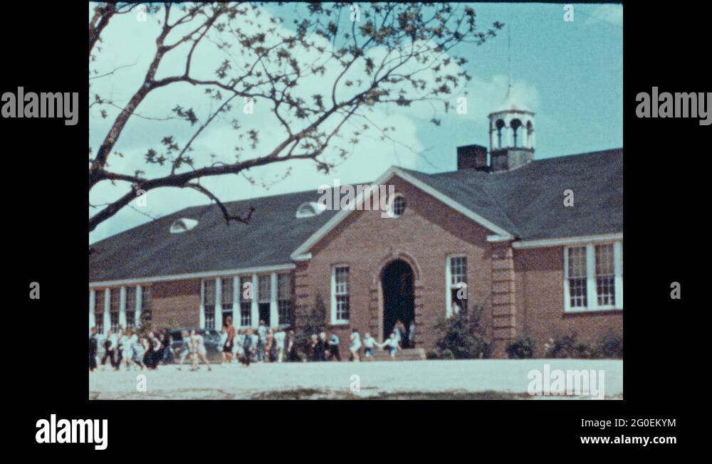 1940s: UNITED STATES: children run out of school. Girl twirls baton in ...