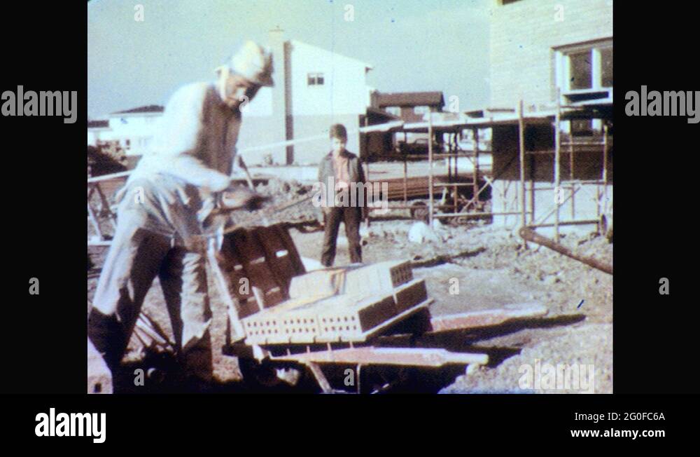 1960s: Construction worker loads bricks on wheelbarrow, boy observes ...