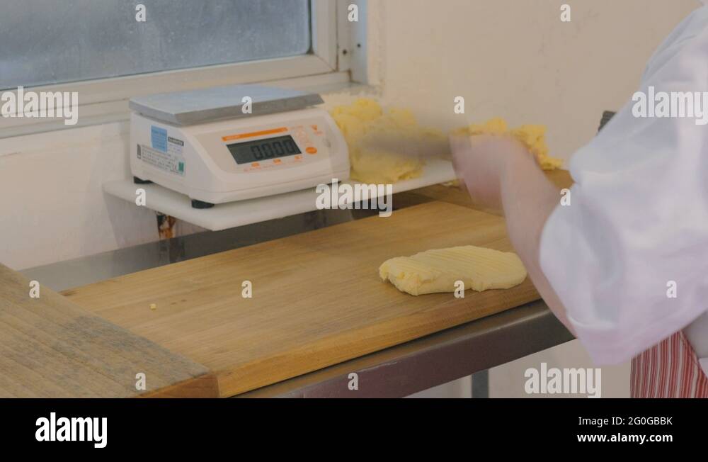 Female factory employee crafting butter with wooden tools on counter ...
