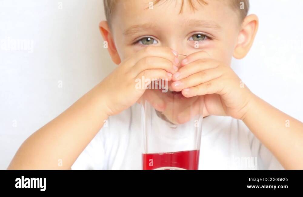 A child drinks juice from a glass beaker on a white background, after ...