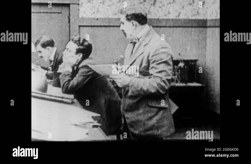 1910s: Man with moustache approaches men at counter. Man points to ...