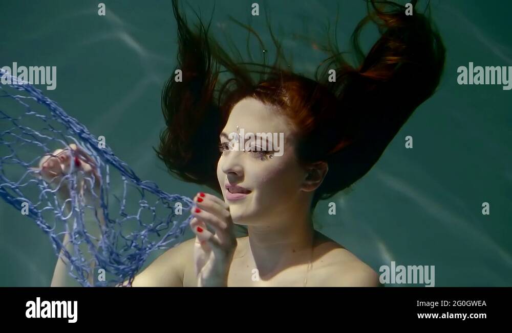 curious mermaid is touching fishing net by hands underwater in ocean in ...