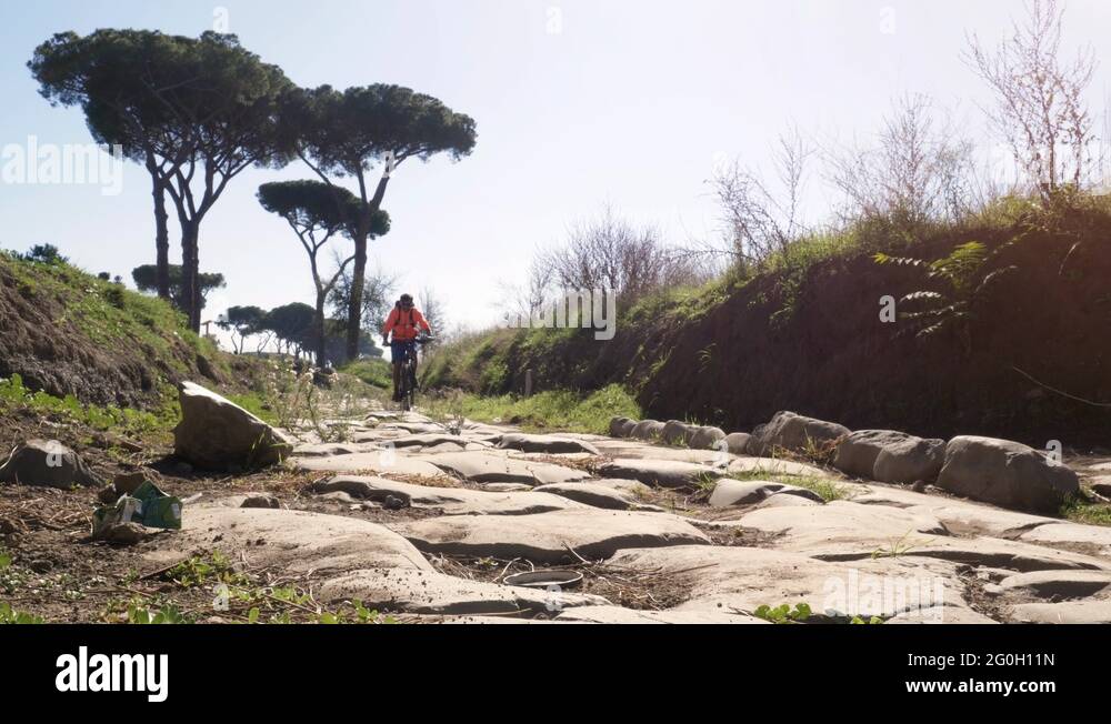 Cyclist riding bike along ancient roman cobblestone road in aqueduct ...