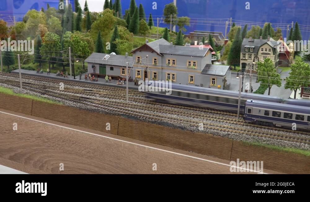 Electric model passenger train moving past station and people ...