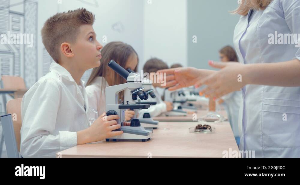 Teacher helps students to adjust the laboratory microscope to work ...