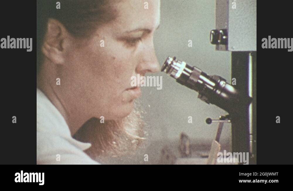 1970s: Woman looks through microscope. Man operates machine that mixes ...