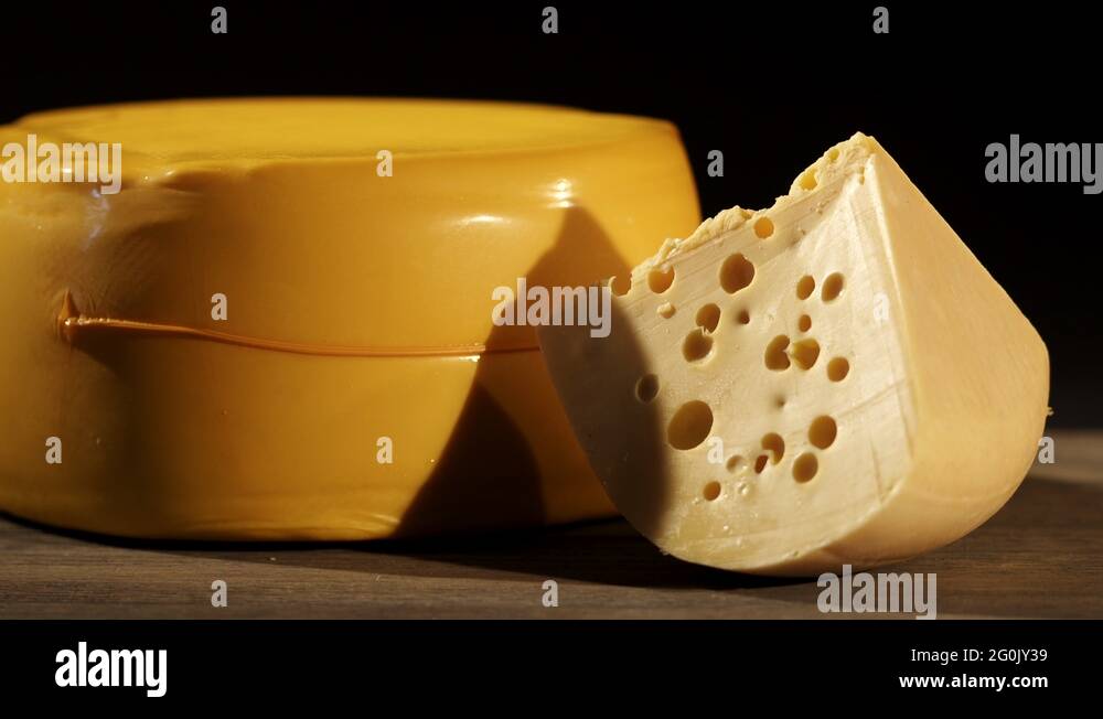 Yellow cheese wheel with wedge of Swiss cheese on an old wooden table ...
