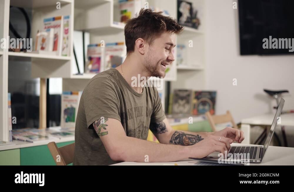 Attractive male programmer at his 20's is laughing while typing ...