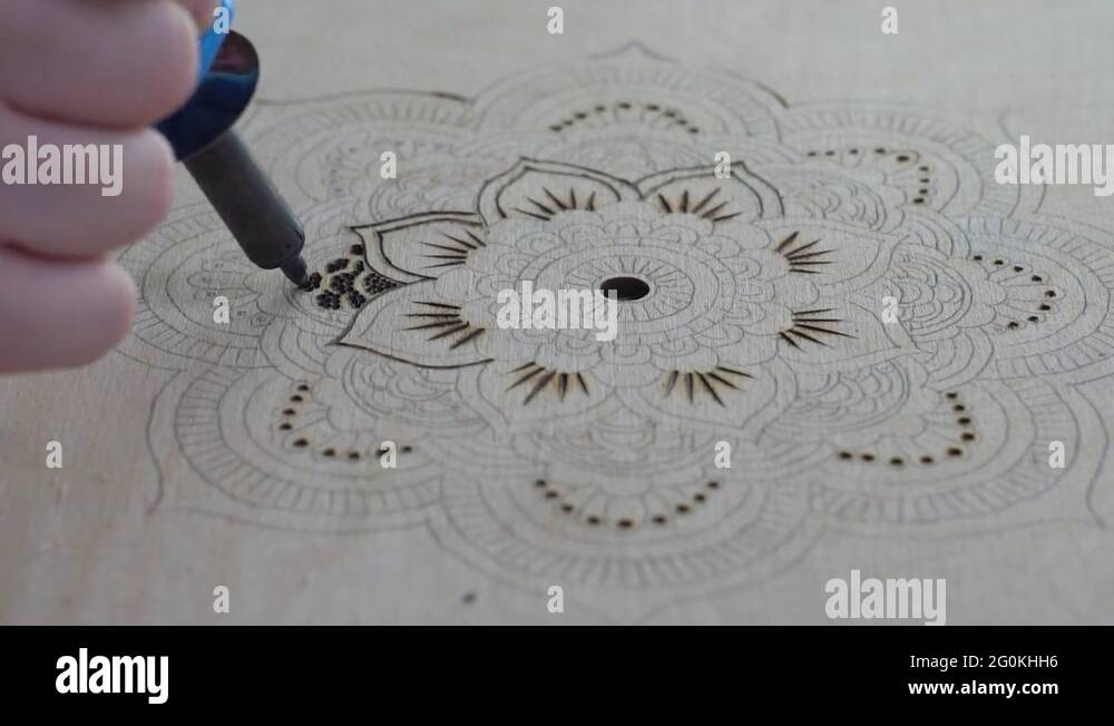 A woman makes pyrography of a flower on a tree, using a dot pattern, a ...