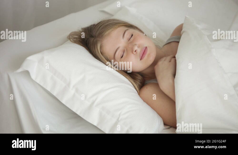 Beautiful young woman sleeping on her back in bed and turning on her ...
