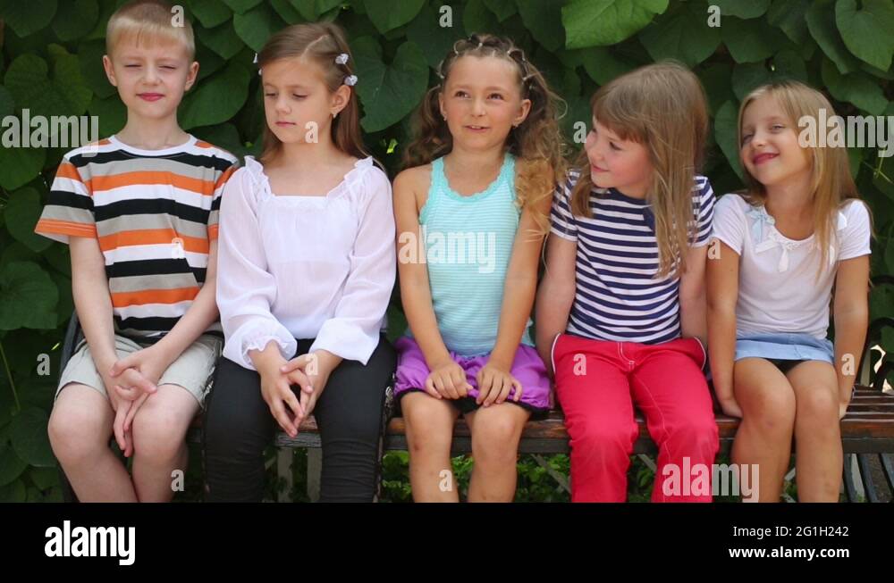 Five happy children sit on bench near green hedge in summer park Stock ...