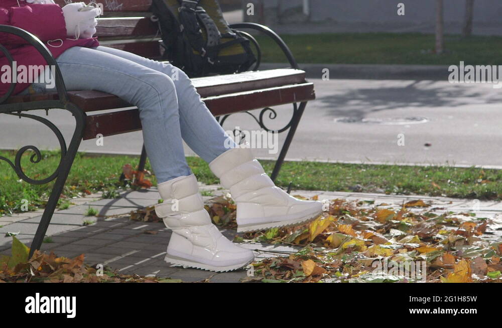 Girl in white boots sitting on the bench wind blows fall foliage Stock ...