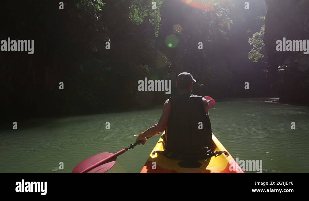 old man back-side view paddles in bright sun rays among cliffs Stock ...