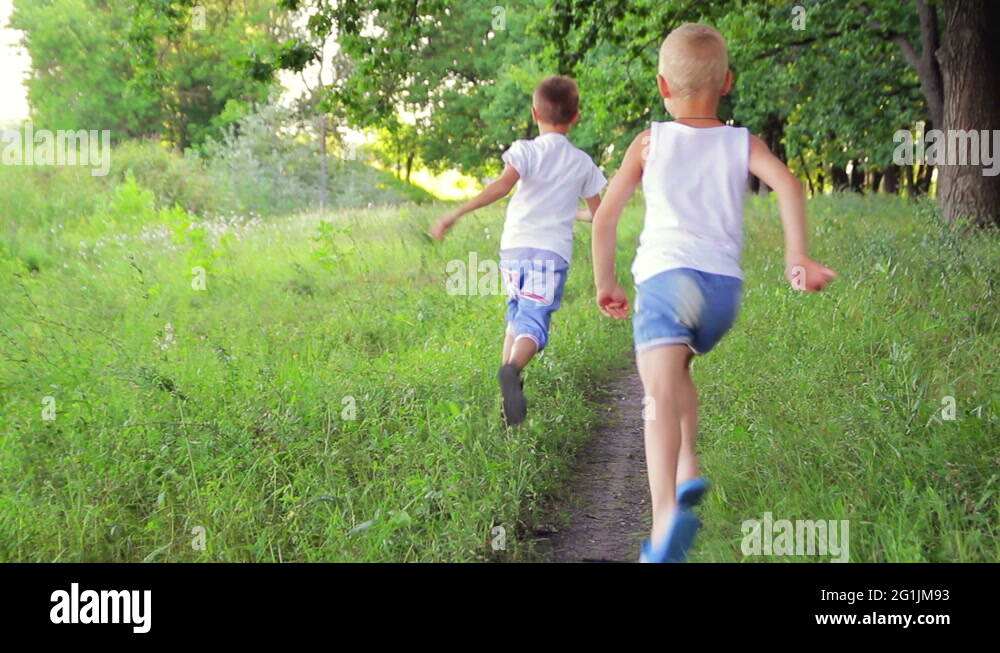 two boys in white clothes running in the park chasing each other ...