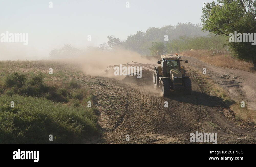 Farmer using modern farm tractor with disk harrows for harrowing field ...
