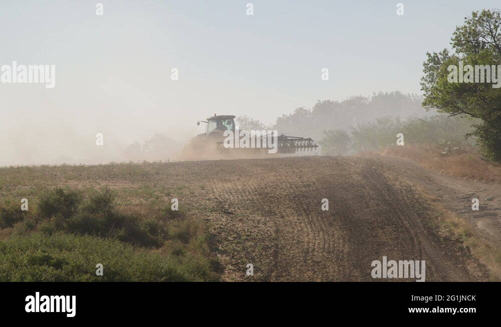 Farmer using modern farm tractor with disk harrows for harrowing field ...