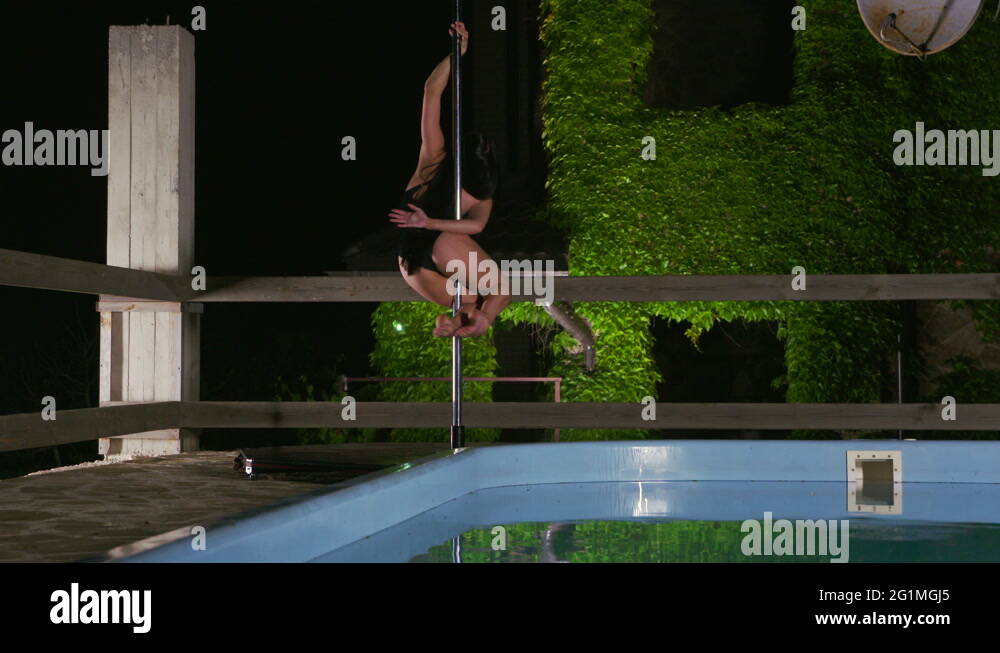 Fit girl poledancer performs fitness pole dance spins beside pool at ...