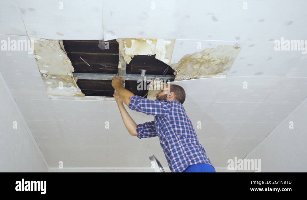 Man repairing collapsed ceiling. Ceiling panels damaged huge hole in ...