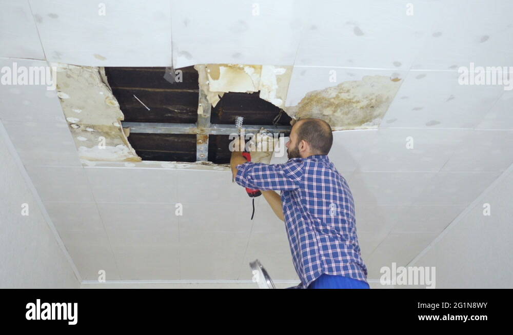 Man repairing collapsed ceiling. Ceiling panels damaged huge hole in ...