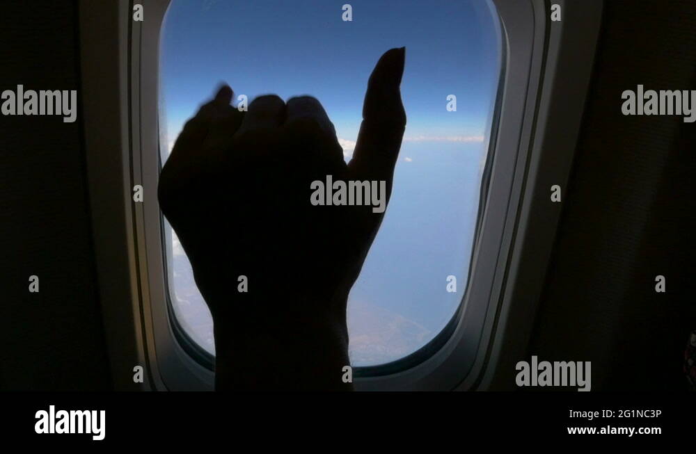 The hand on the background of the airplane window says goodbye to the ...