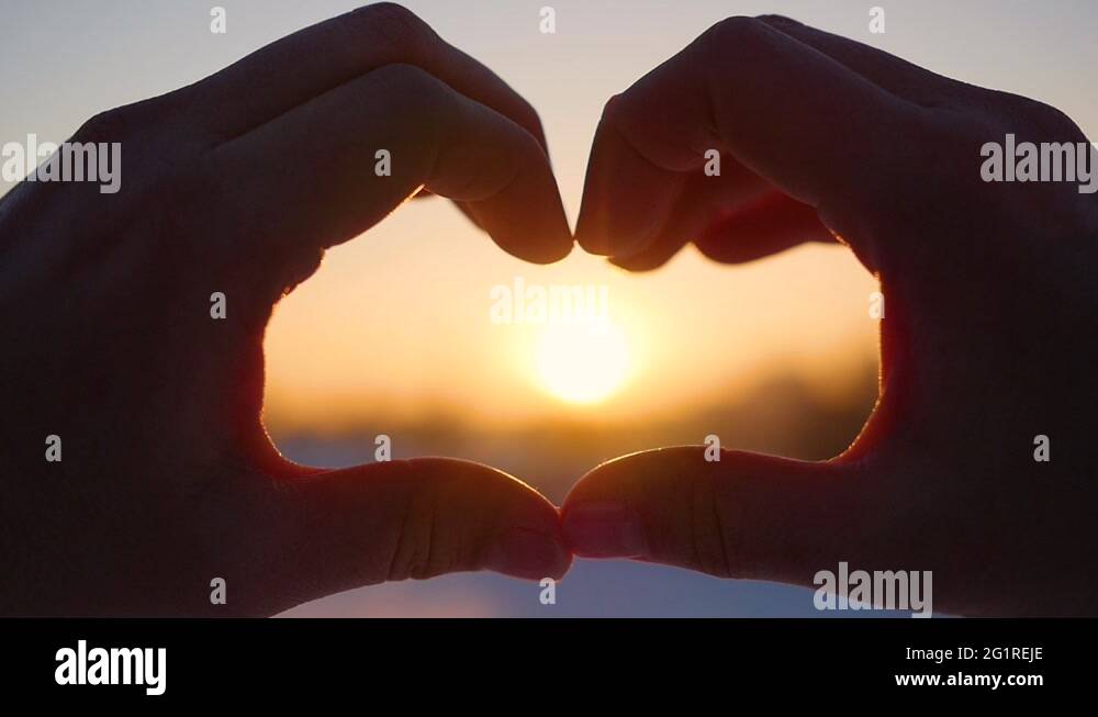 girl making heart with hands in the sun. Silhouette hand in heart shape ...