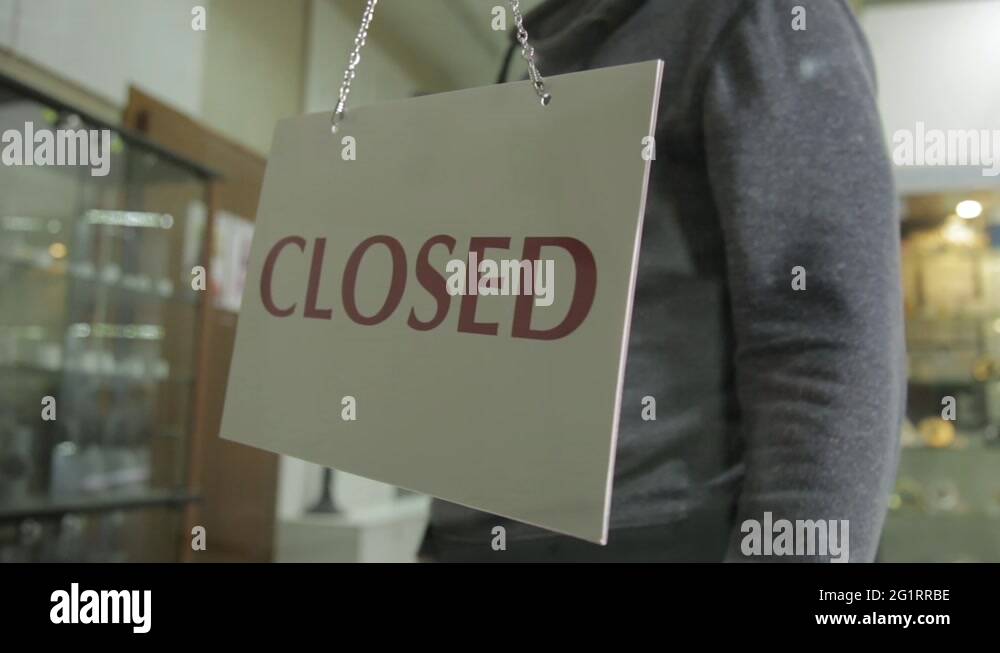 open sign is turned to closed in a storefront window. man flipping ...