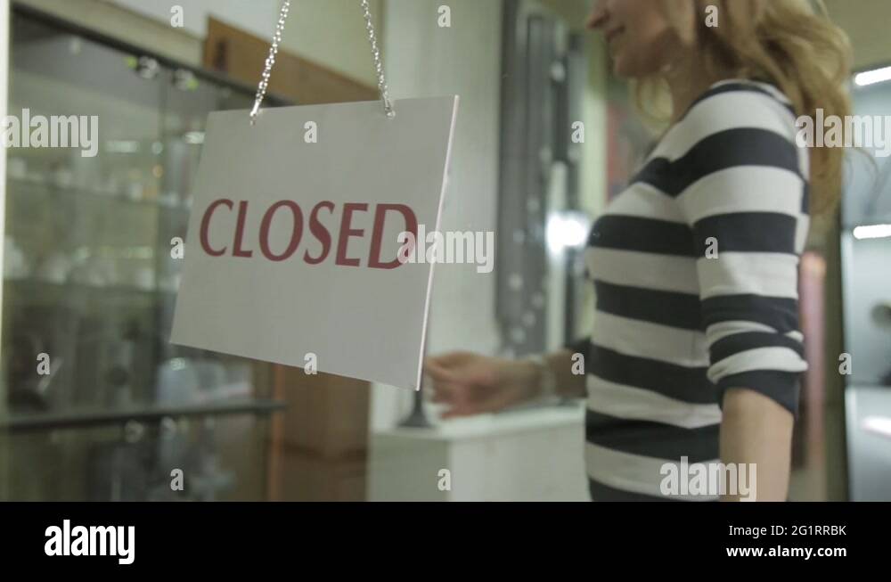 open sign is turned to closed in a storefront window. woman flipping ...