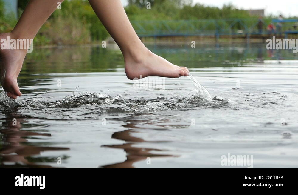 Female legs are swinging over some lake waters in a relaxed way in slow ...