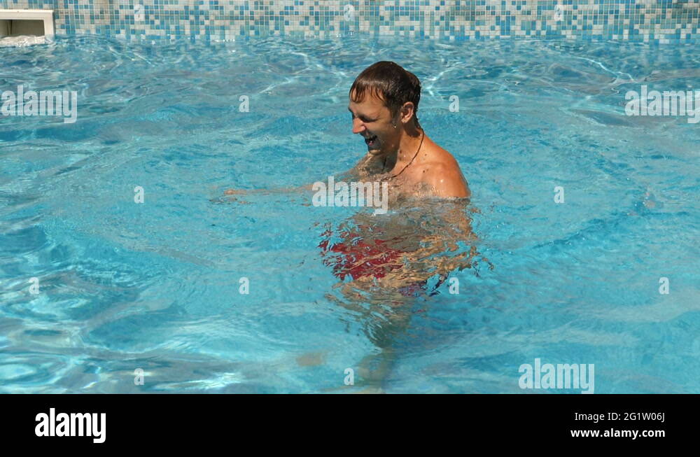 A man dives into the pool with blue water. Splashes fly in different ...