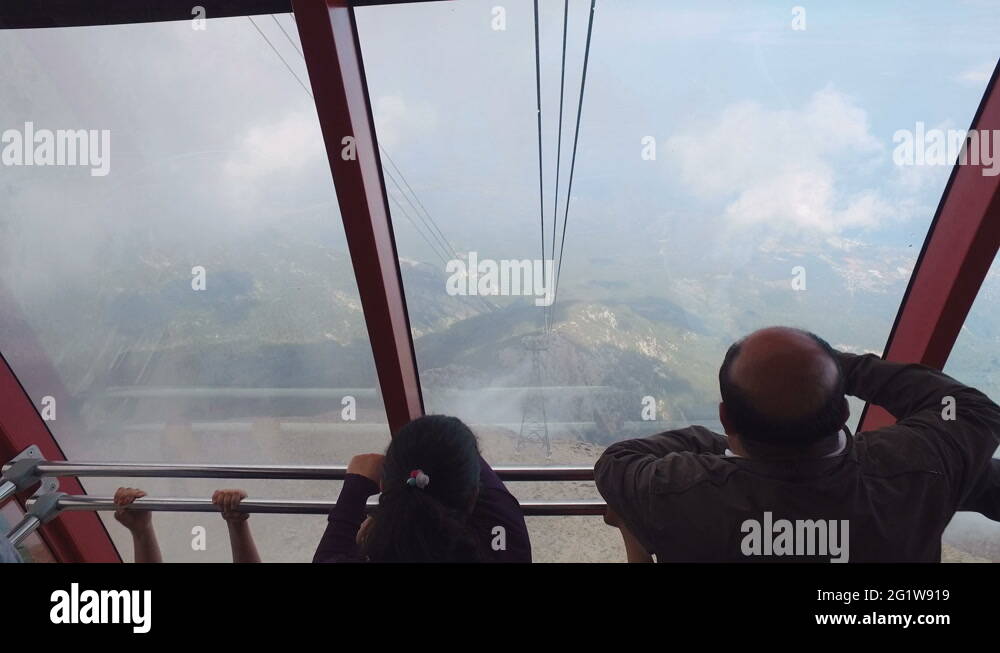 people are inside cabin of cable car, looking down from top of mountain ...