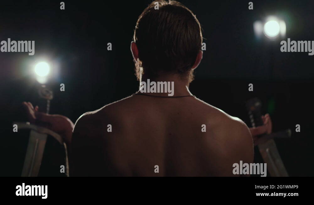 Portrait of strong man workouts with swords on the light of dark ...