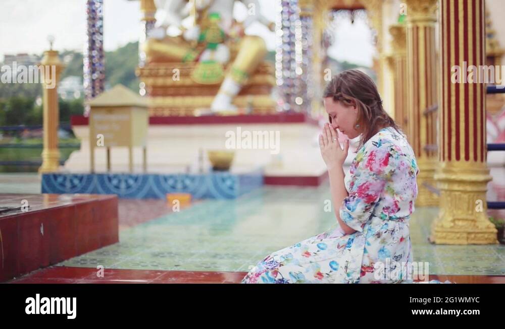 Young religious woman coming in temple prays on the knees at complex ...