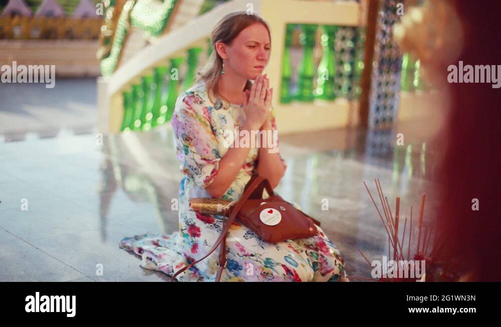 Young sad woman coming in temple prays on the knees at complex Wat Plai ...