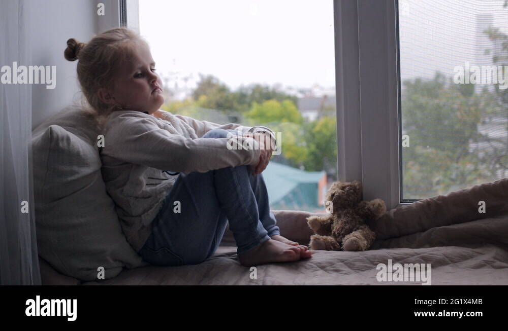 Sad cute young girl sitting on a window sill Stock Video Footage - Alamy