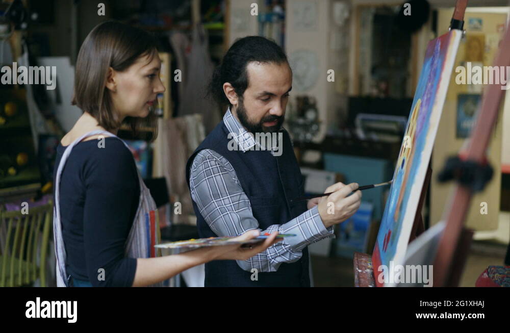 Skilled artist man teaching young girl to draw paintings and explaining ...