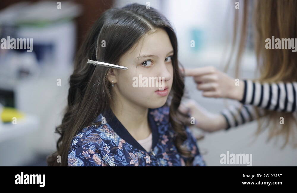 Hairdresser makes the final stage of creating a hairstyle for a cute ...