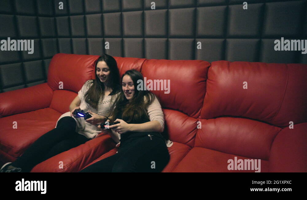 Two Young Girls Playing Video Games With Game Controller On Red Sofa 6103