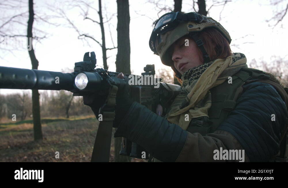 Young pretty redhead woman in military uniform armed with rifle at the ...