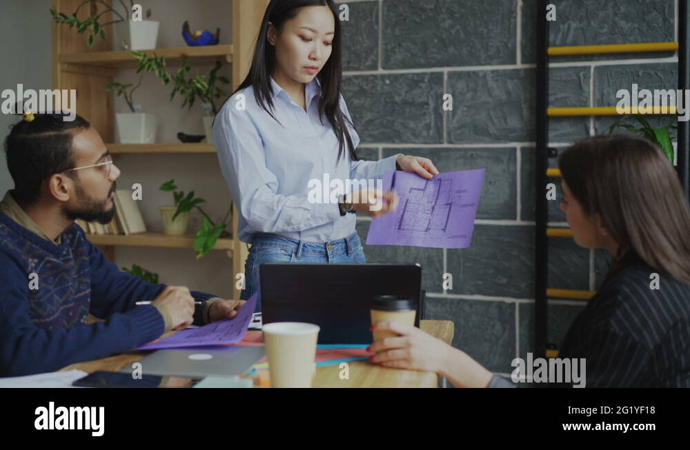 Young asian woman presenting paper architectural plan of house to multi ...
