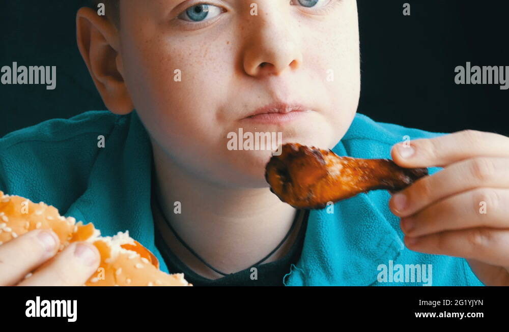 Teen alternately eating a hamburger and greasy fried chicken wings in ...