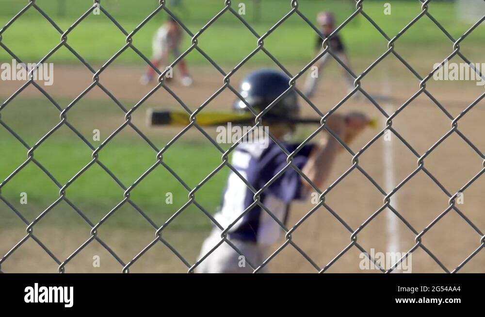 Boys play in a little league baseball game through a chain-link fence ...