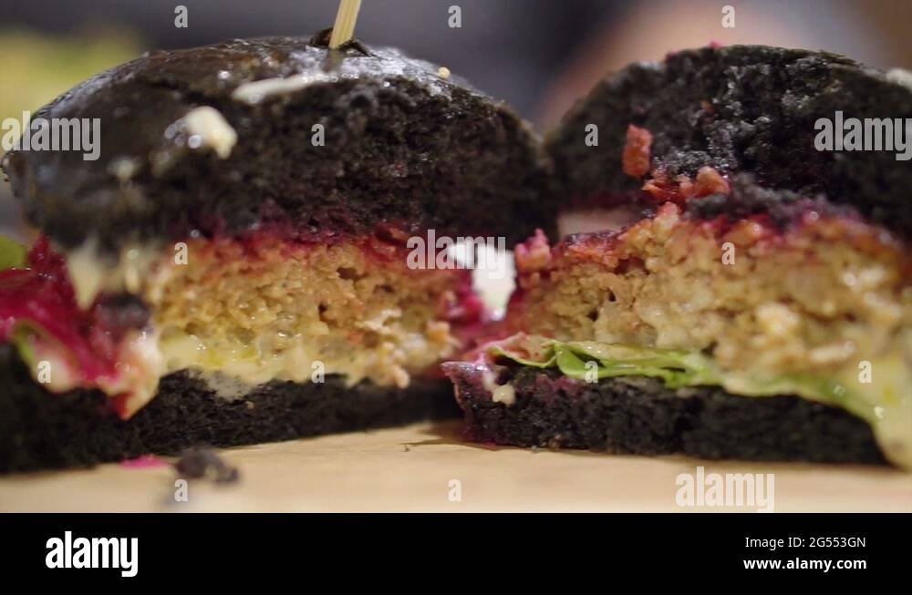 Charcoal beef black burger cut in half showing juicy meat and vegetable ...