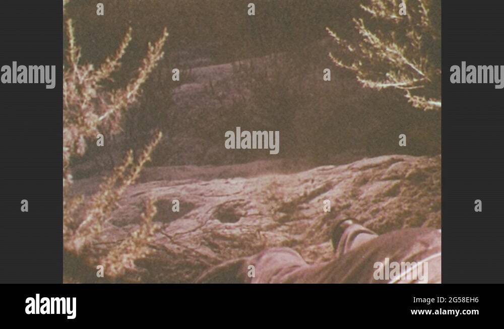 1970s: Teen boy stuck on rocky cliff. Legs dangle in air as rock ...