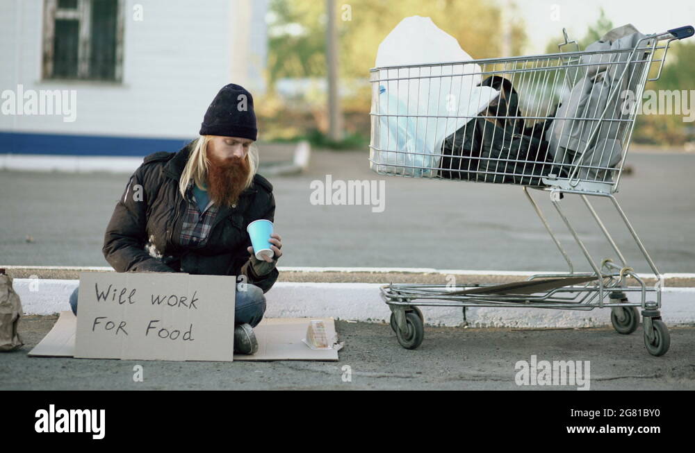 Homeless young man counting how much money he got holding paper cup in ...
