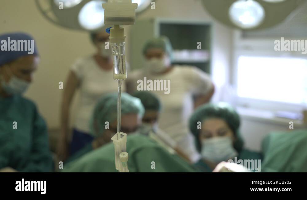 Iv drip close up, surgical team operating in operation room, rack focus ...